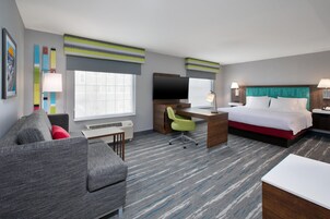 Quarto de hotel com cama, escrivaninha, cadeira e televisão.