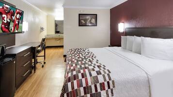 Quarto de hotel com cama, escrivaninha, cadeira, televisão e quadro na parede.