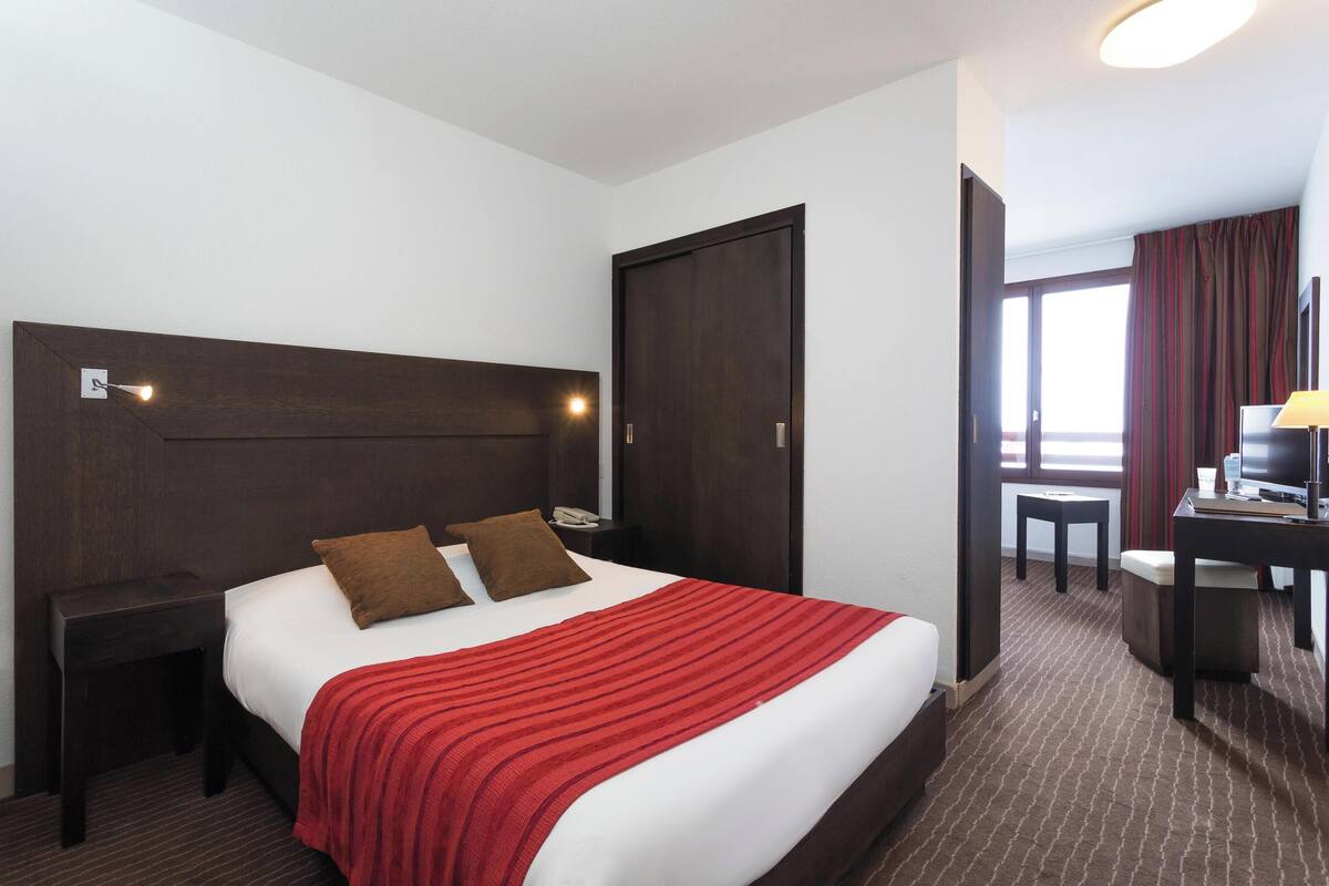 Quarto de hotel com uma cama grande, uma escrivaninha e uma cadeira.