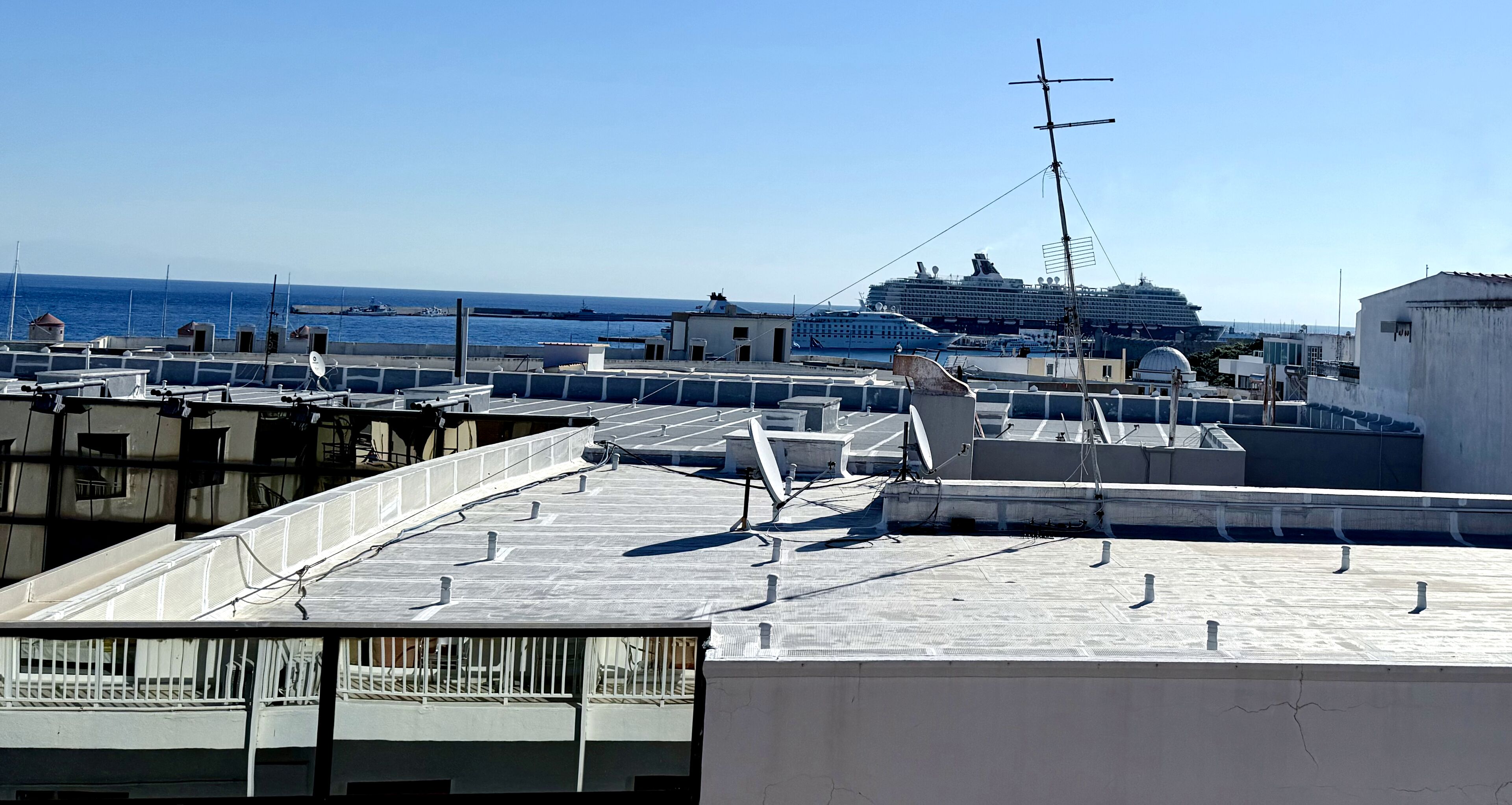 Terraço com vista para o mar e um navio de cruzeiro ao fundo.