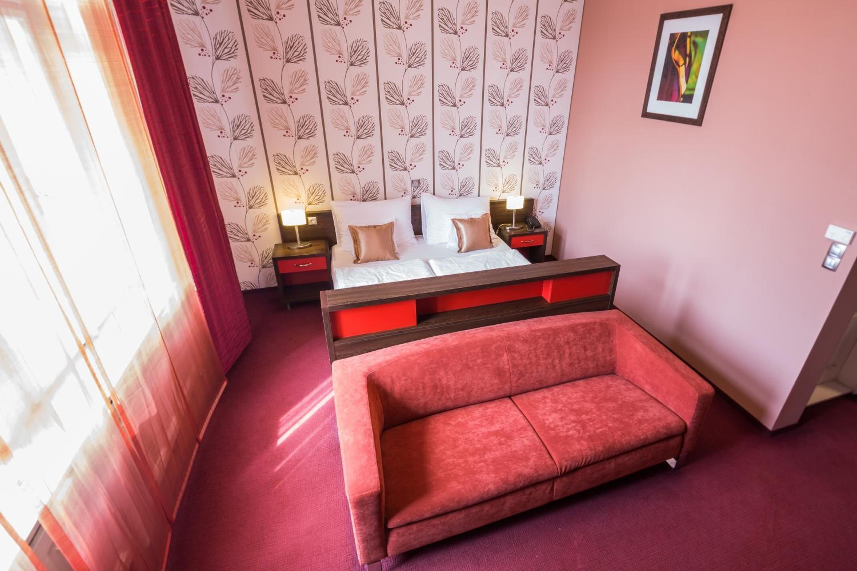 Um quarto com uma cama, duas mesas de cabeceira, um sofá vermelho e um papel de parede estampado.