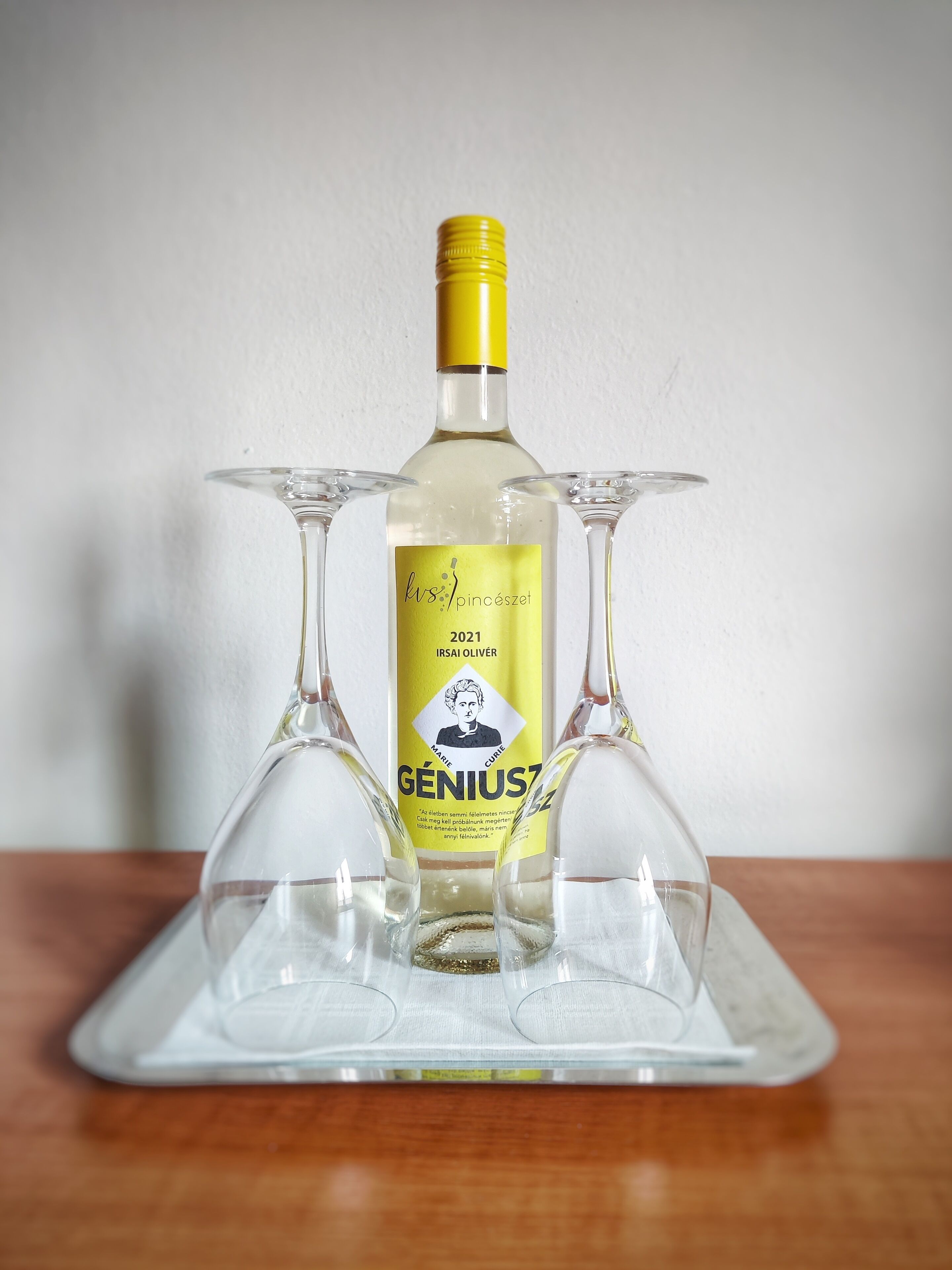 Uma garrafa de vinho Geniust com dois copos de vinho vazios em um tabuleiro.