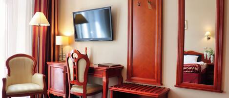 Quarto de hotel com televisão, escrivaninha com luminária, duas cadeiras, armário e um espelho grande.