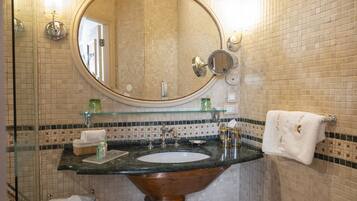 Um banheiro com um espelho oval grande, uma pia com pedestal de cobre e uma prateleira de vidro acima da pia.