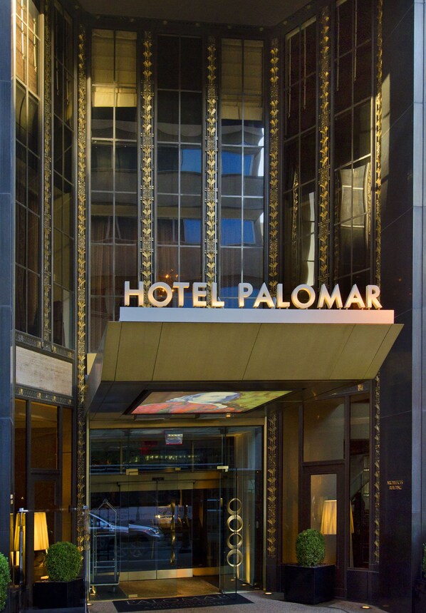 Entrada do Hotel Palomar, com fachada moderna, grandes janelas de vidro e uma placa bem visível sobre a entrada.