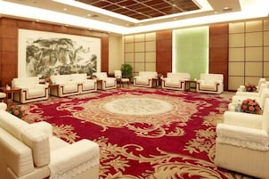 Uma sala de conferências com um tapete vermelho grande, cadeiras brancas e um quadro grande na parede.