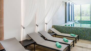 Um salão de spa com cadeiras reclináveis, uma piscina em vidro e vista para o verde lá fora.