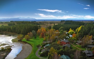 Paisagem rural com rio, casas e montanhas ao fundo.