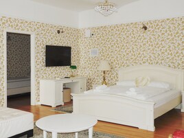 Quarto com cama, escrivaninha, cadeira, televisão e lustre.