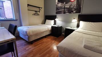 Quarto de hotel com duas camas, uma escrivaninha e uma janela.