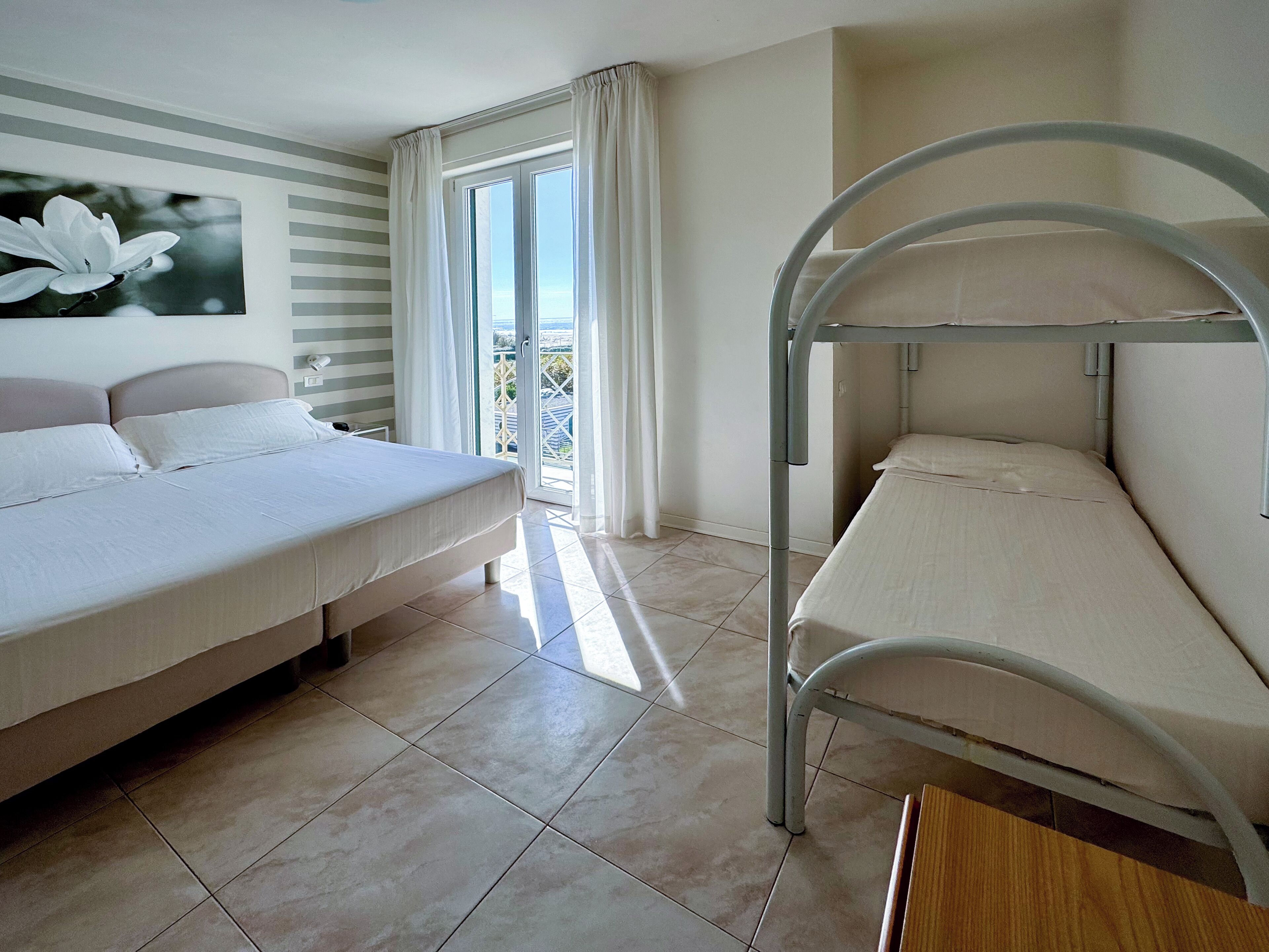 Quarto de hotel com cama, beliche, vista para o exterior e um quadro na parede.