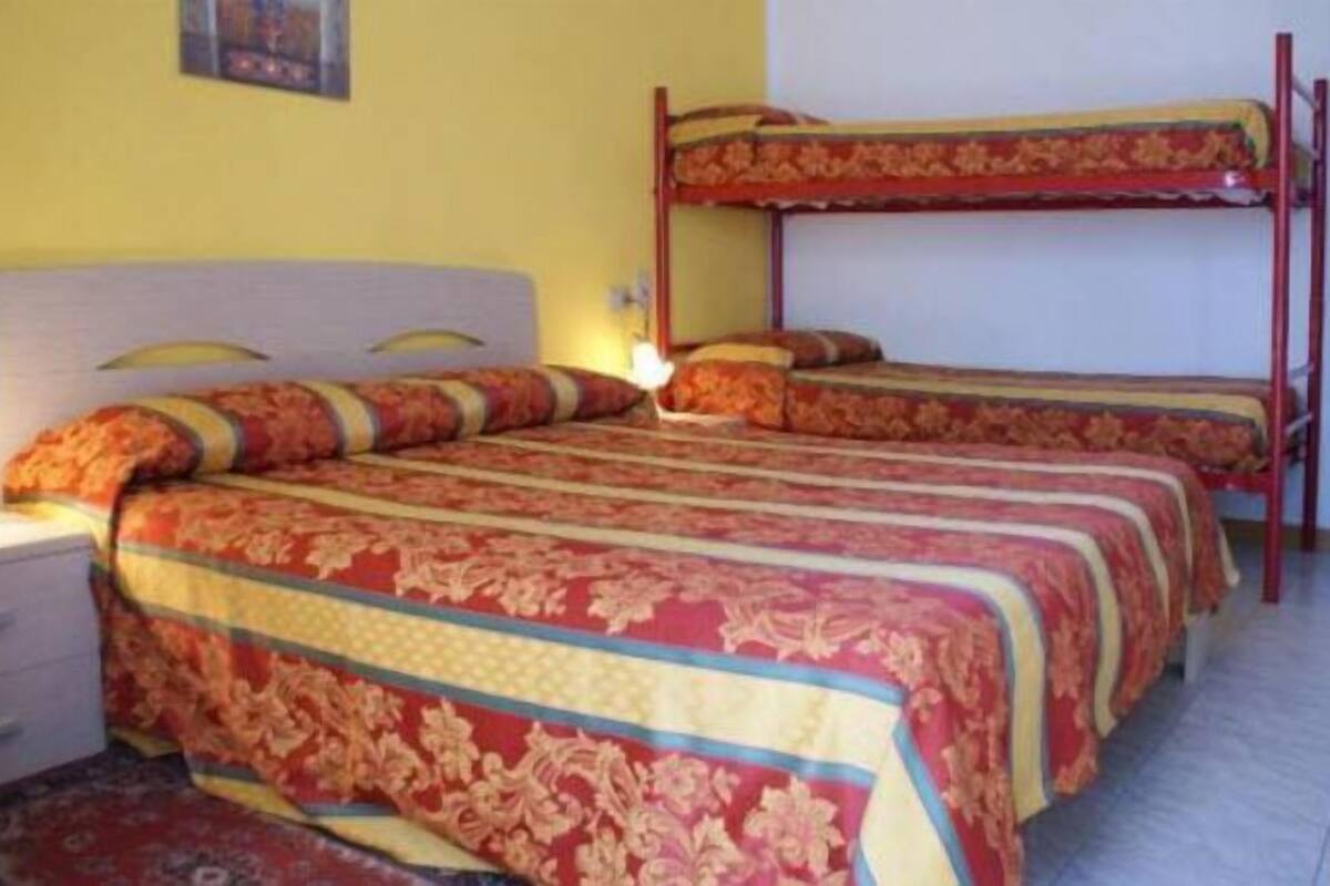 Quarto com duas beliches, cada uma com colcha e almofadas estampadas. Há uma mesa de cabeceira com abajur e uma gaveta.
