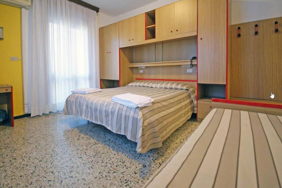 Quarto com cama, guarda-roupa de madeira e uma pequena escrivaninha.