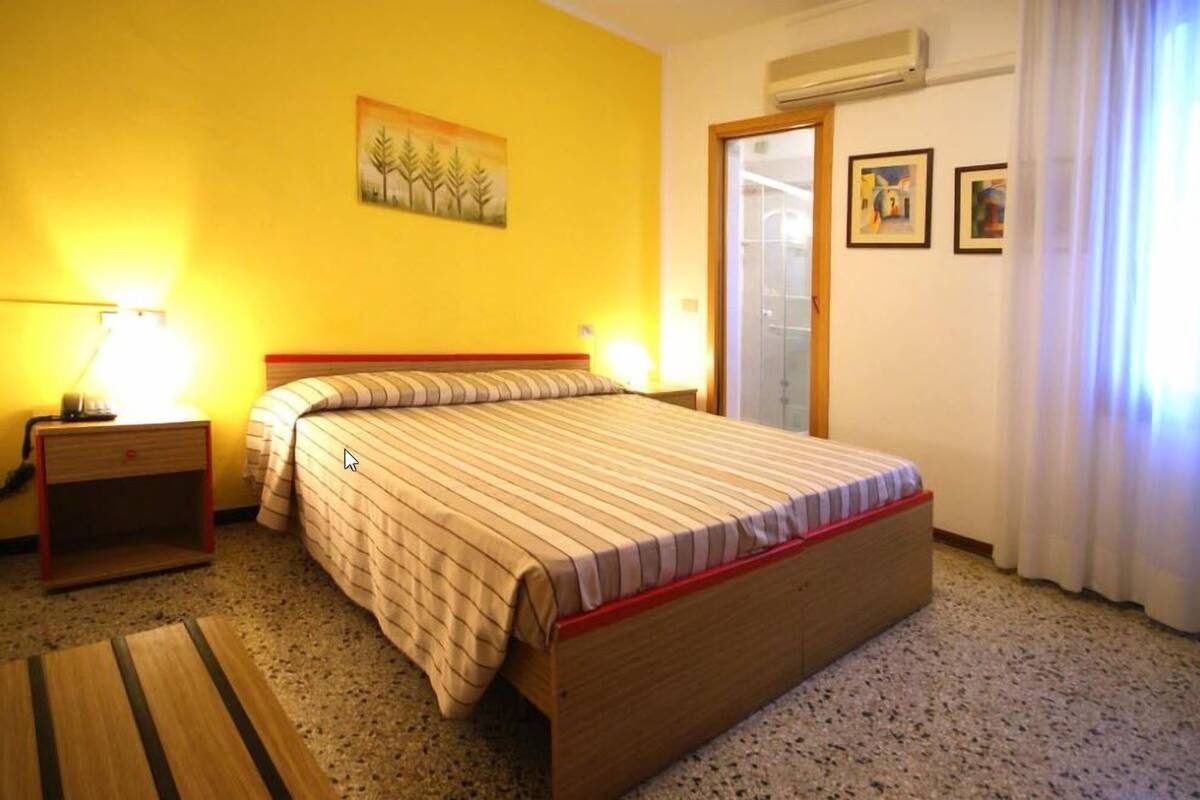 Quarto com cama, mesas de cabeceira, um quadro e uma porta com vista.