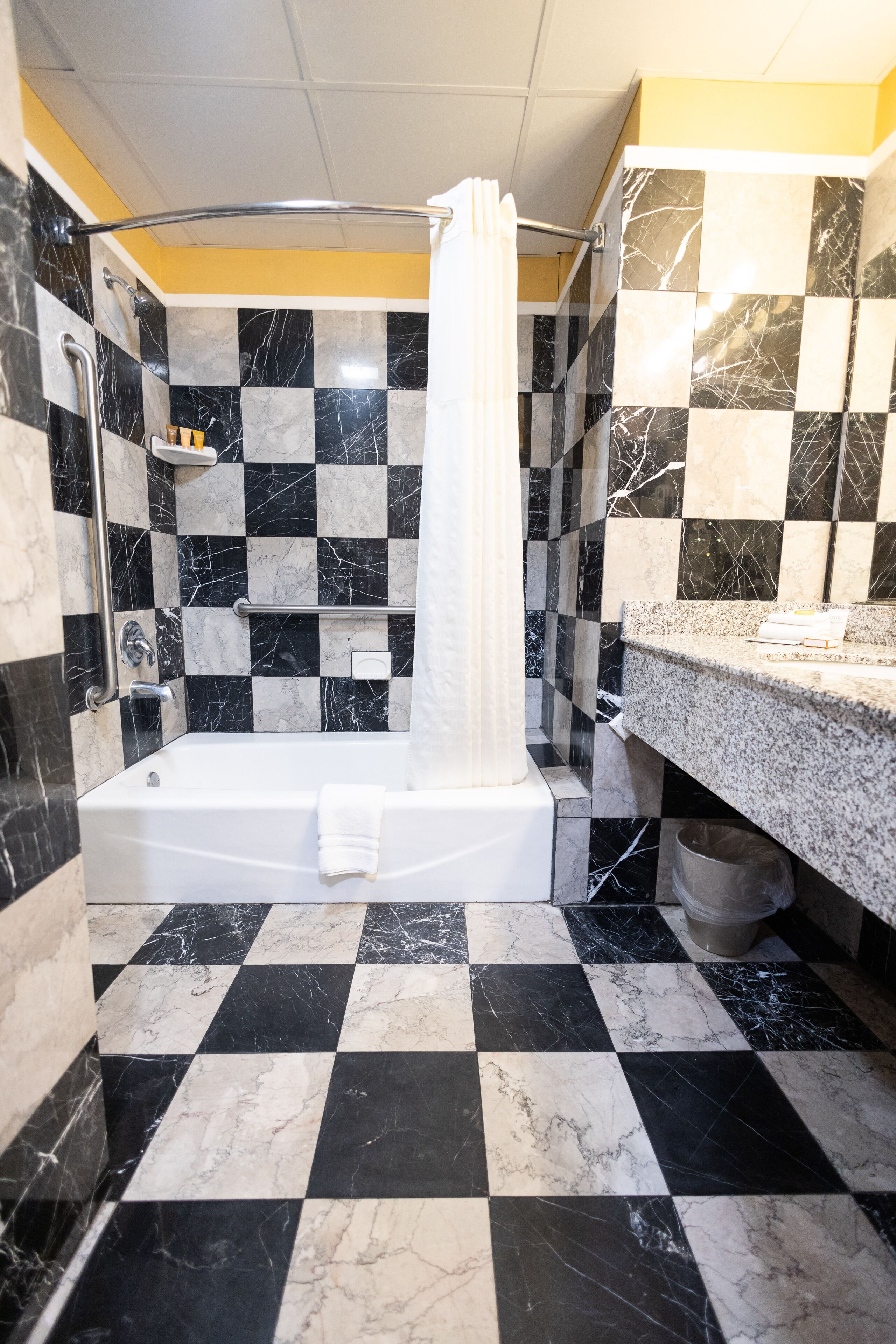 Um banheiro com piso de mármore quadriculado em preto e branco, uma banheira branca e uma pia com bancada de mármore.