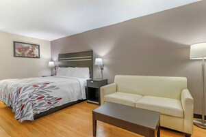Quarto de hotel com cama, sofá, mesa de cabeceira, abajur e mesa de centro.