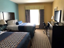 Quarto de hotel com duas camas, uma escrivaninha com computador, televisão e janela com cortinas.