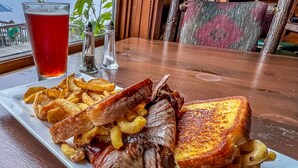 Uma refeição com batatas fritas, um sanduíche e um picles no prato, com uma bebida e saleiros e pimenteiros na mesa.