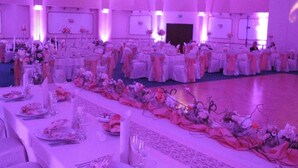 Salão de banquetes com mesas redondas dispostas para um evento formal, com toalhas brancas e arranjos florais.