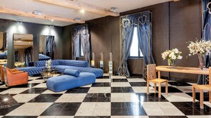 Uma sala de estar espaçosa com piso xadrez, um sofá seccional azul e uma mesa de jantar de madeira com cadeiras.