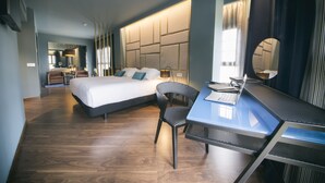 Quarto de hotel moderno com uma cama grande, uma escrivaninha com cadeira, um espelho e vista para a cidade.