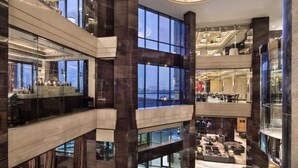 Um saguão de hotel com vários níveis, fachada de vidro, área de bar e espaço de estar com sofás.