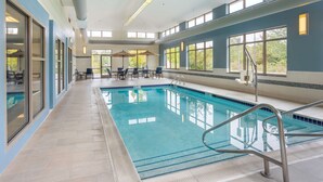 Piscina com água azul cristalina, rodeada por um deck revestido e grandes janelas.