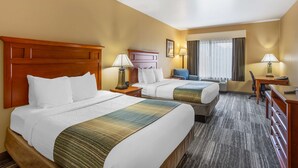Quarto de hotel com duas camas, uma escrivaninha, uma cadeira e uma janela com cortinas.