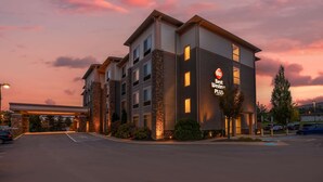 Um hotel com vários andares, com a placa 'Best Western Plus', um estacionamento e céu claro ao entardecer.