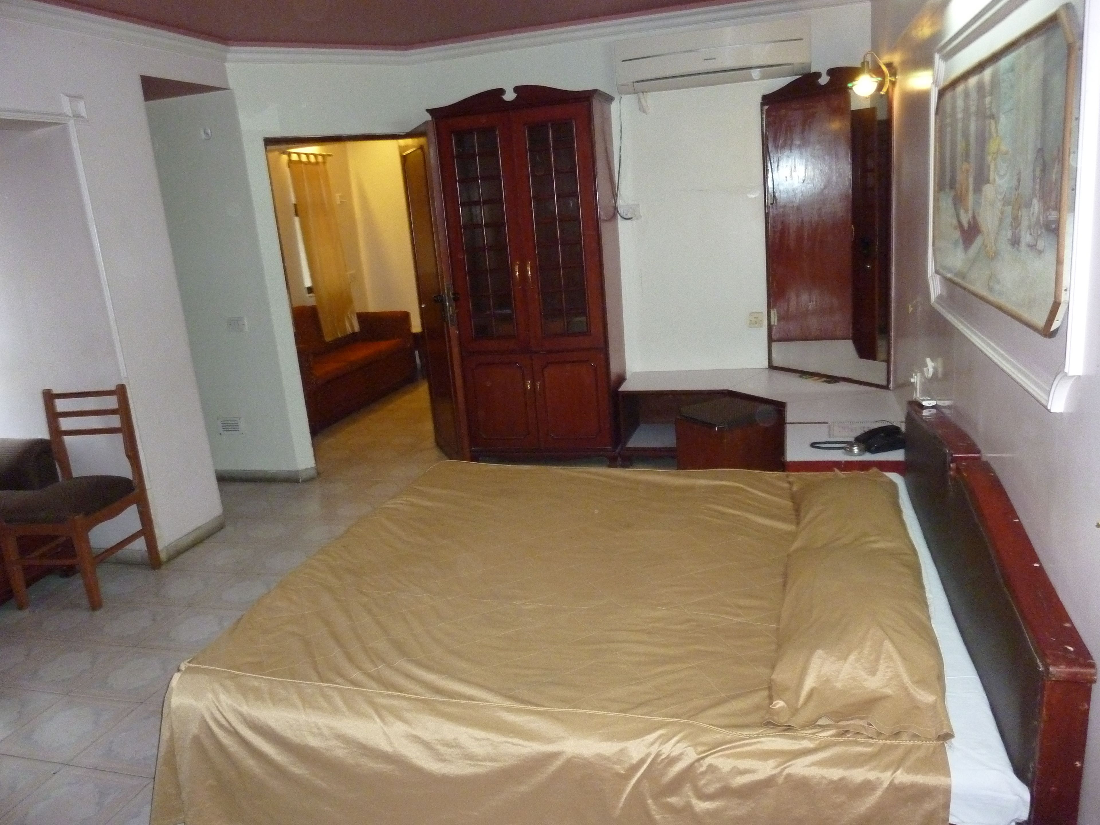 Quarto com cama, guarda-roupa de madeira, cadeira e escrivaninha.