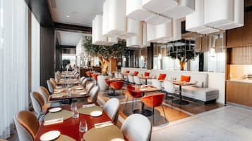 Um restaurante moderno com mesas comunitárias alongadas, cabines individuais e uma combinação de cadeiras vermelhas e cinzentas.