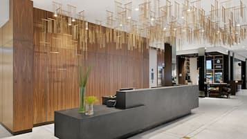 Uma área de recepção moderna com parede de painel de madeira, balcão de recepção escuro e luminária pendente.