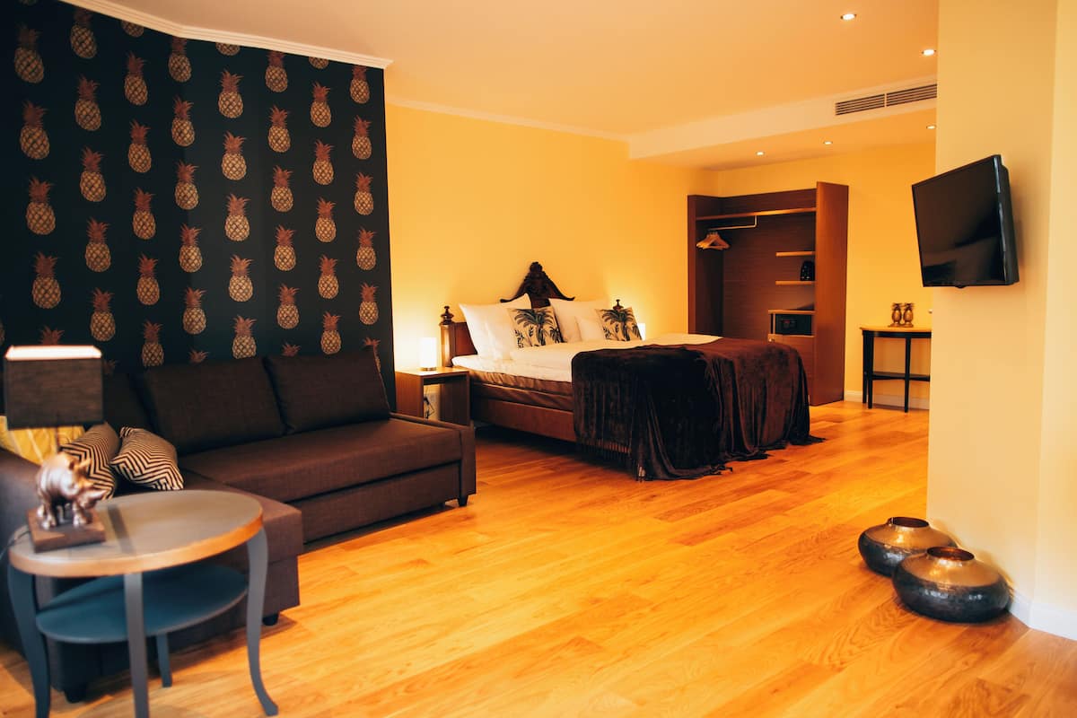 Quarto de hotel com cama, sofá, uma mesa pequena e televisão.