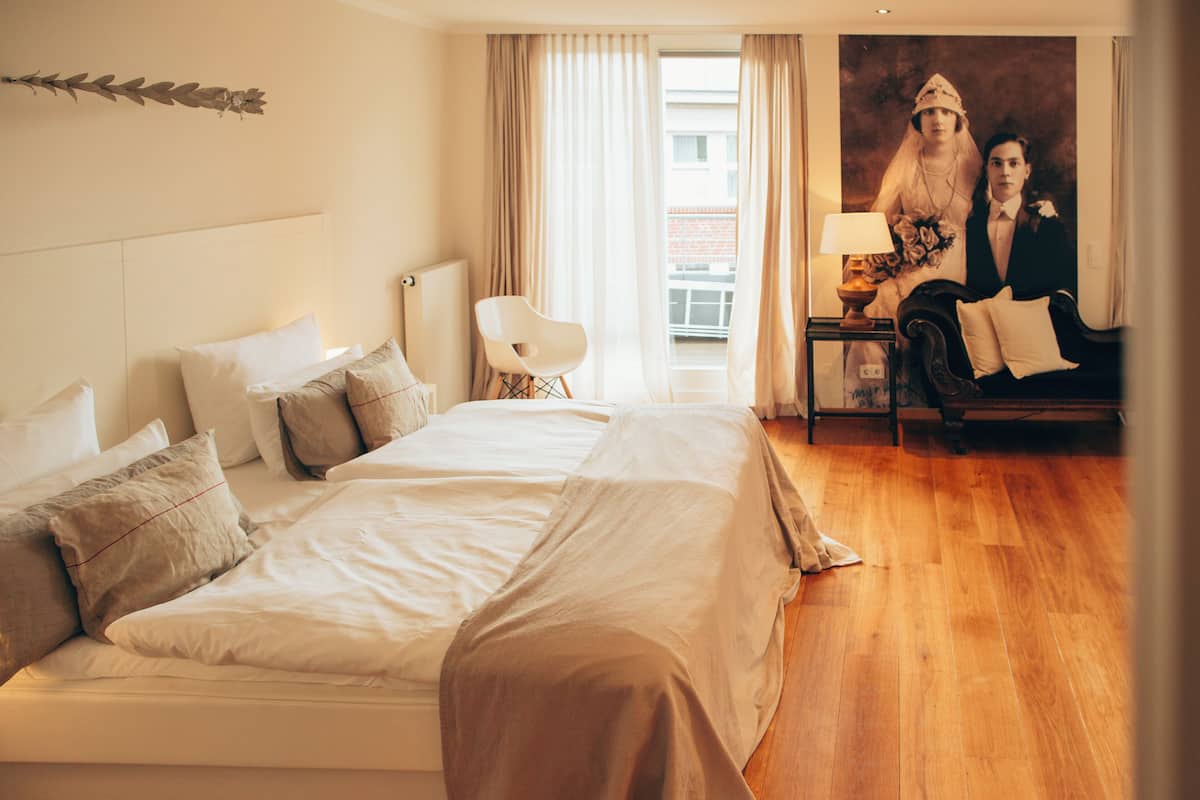 Quarto de hotel com duas camas, um espaço de estar com uma poltrona e uma mesa, e uma fotografia grande emoldurada na parede.