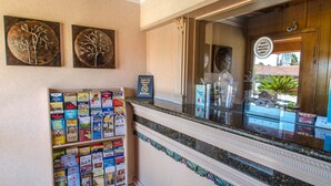 Uma área de recepção com balcão de mármore, estante de livros de viagem e duas pinturas penduradas na parede.