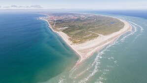 Vista aérea de uma área costeira com praia, paisagem urbana e céu limpo.