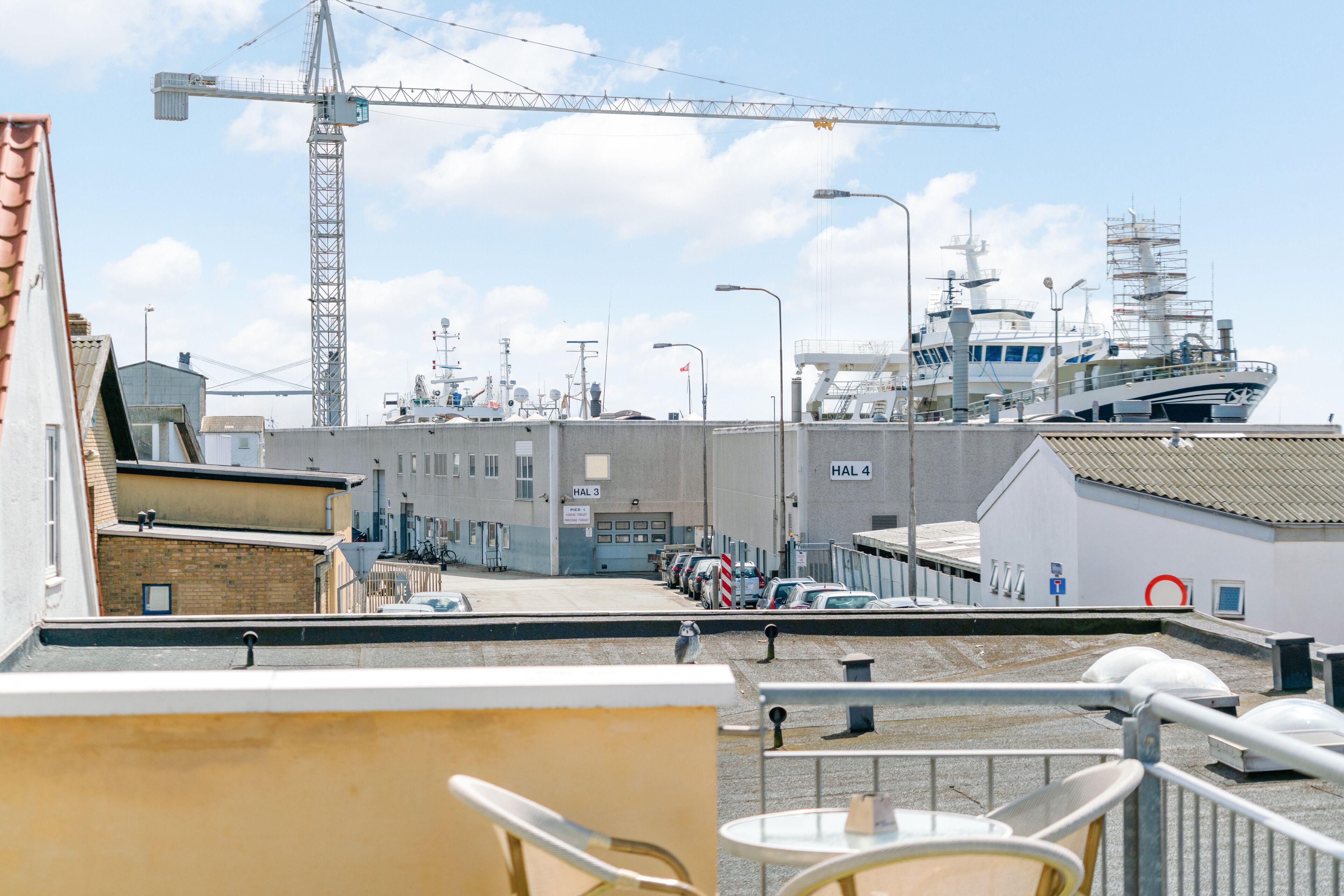 Terraço no telhado com vista para um porto, incluindo uma grande grua e um iate.