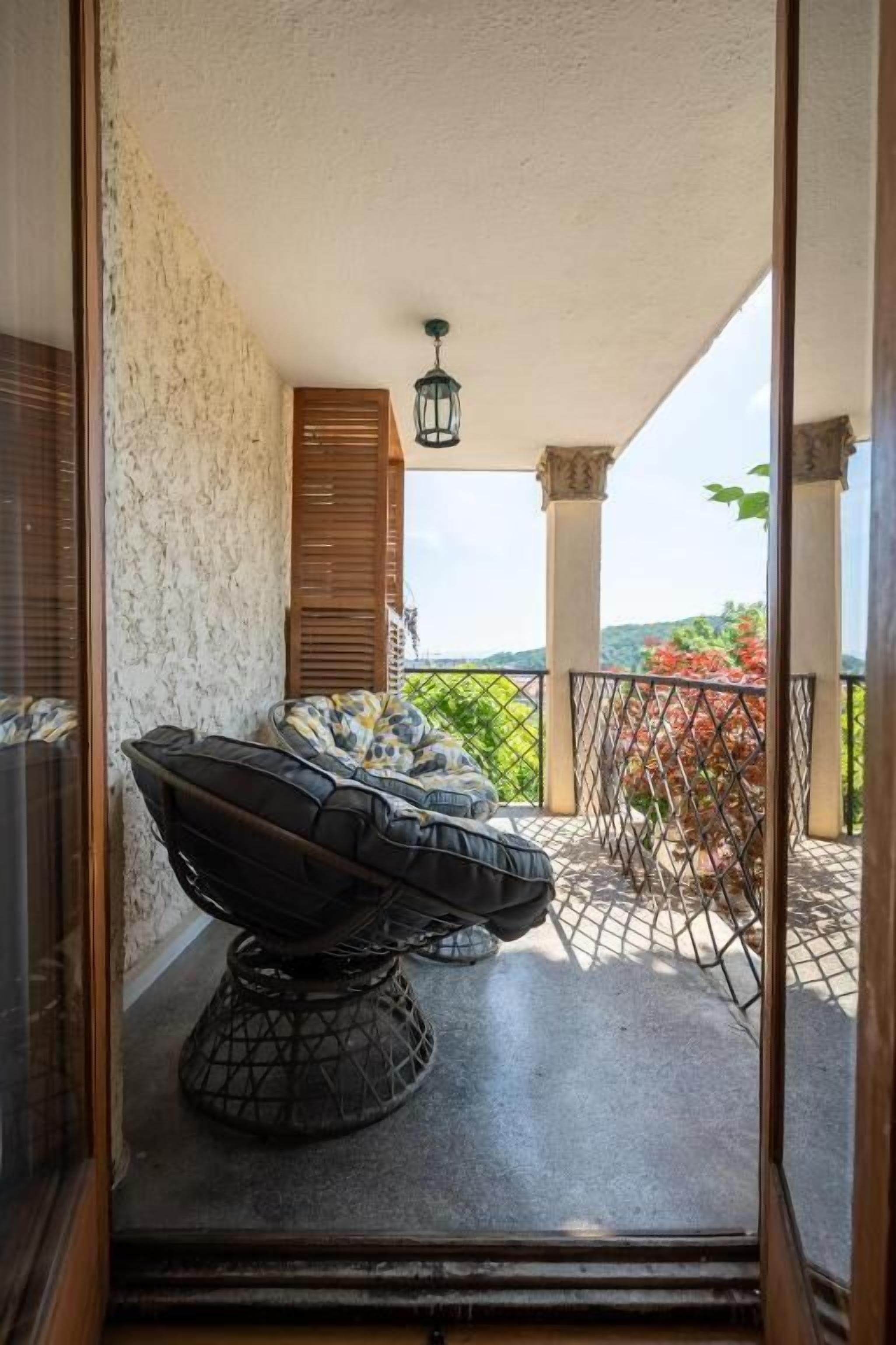 Uma varanda com uma poltrona preta, um toldo de madeira e vista para o verde.