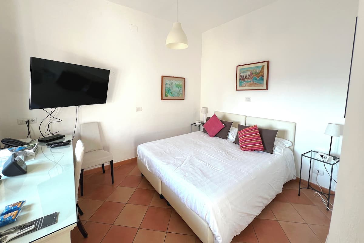 Quarto de hotel com uma cama, uma escrivaninha com televisão e duas pinturas na parede.