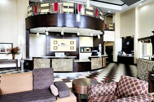 Um saguão de hotel com balcão de recepção, área de estar e parede decorativa.