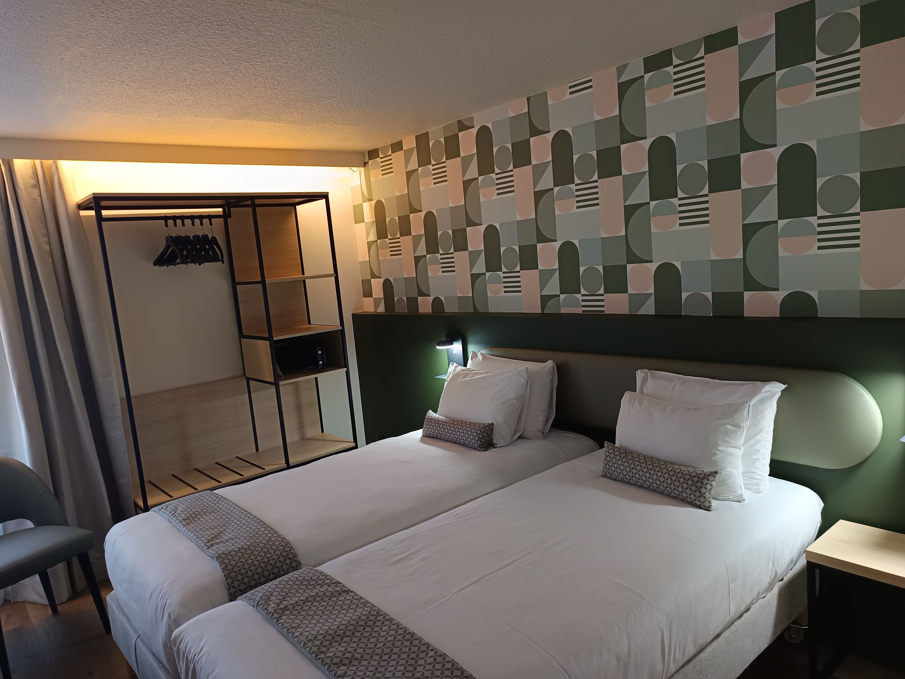 Quarto de hotel com uma cama grande, uma escrivaninha, uma cadeira e um guarda-roupa.