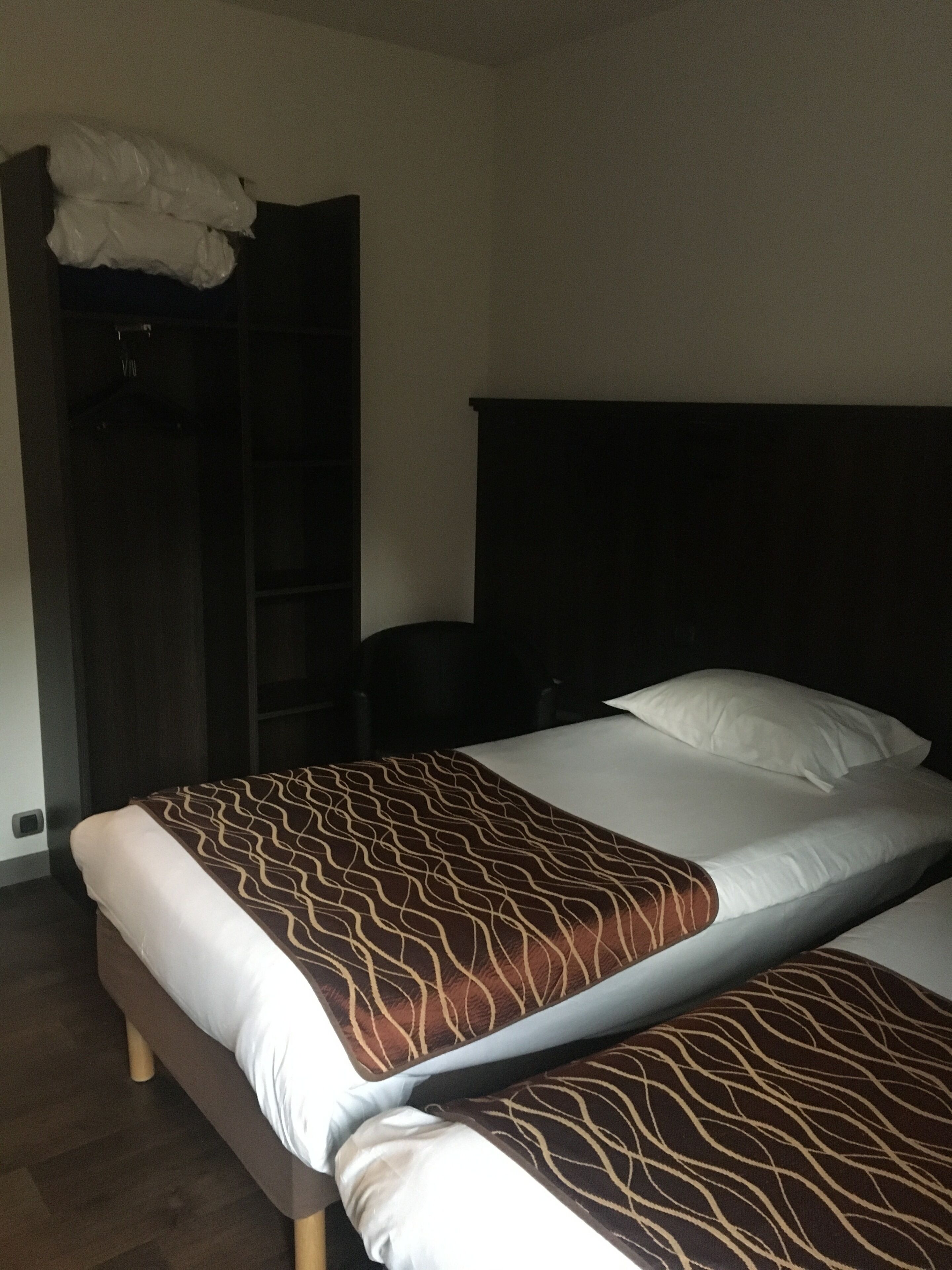 Quarto de hotel com duas camas, um guarda-roupa e uma secretária.