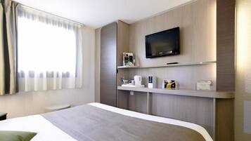 Quarto de hotel com cama, televisão na parede, mesinha e janela com cortinas.