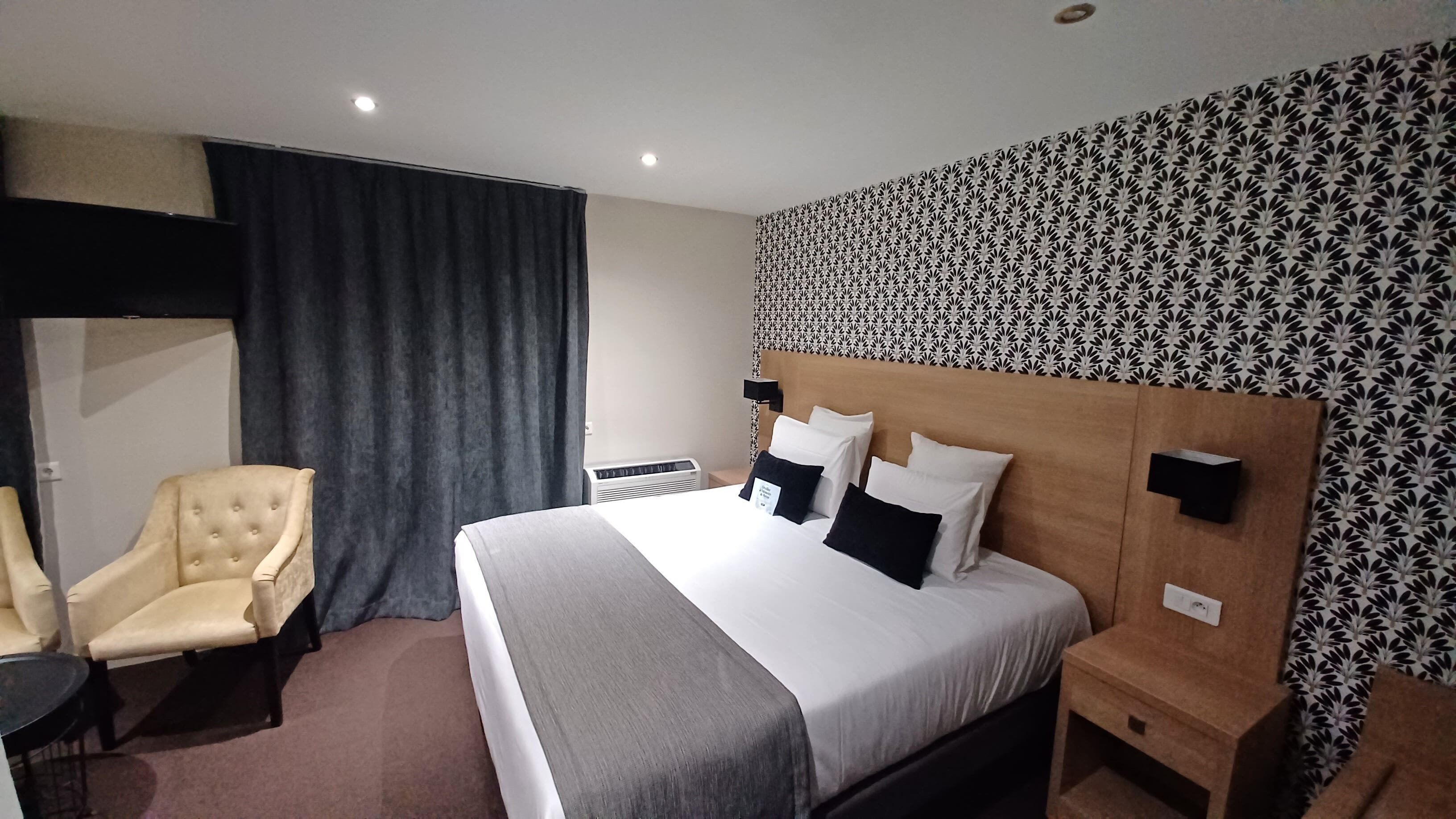 Quarto de hotel com uma cama grande, uma cadeira, uma escrivaninha e parede estampada.