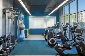 Uma academia com equipamentos de ginástica, uma janela grande e uma parede azul.