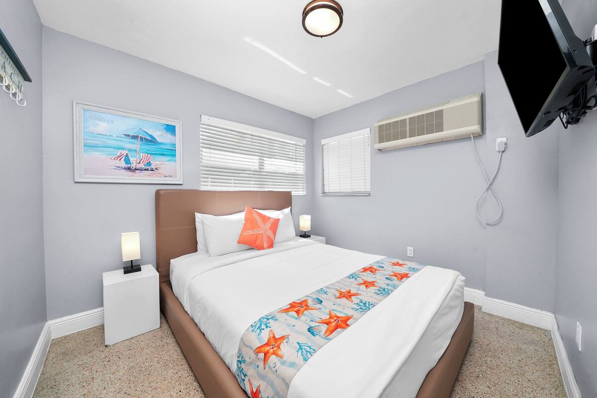 Quarto com cama, mesas de cabeceira, um quadro, iluminação no teto e um aparelho de ar condicionado.