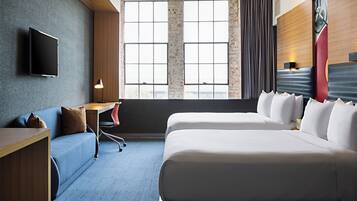 Quarto de hotel com cama, escrivaninha, cadeira, televisão e uma grande janela com cortinas.
