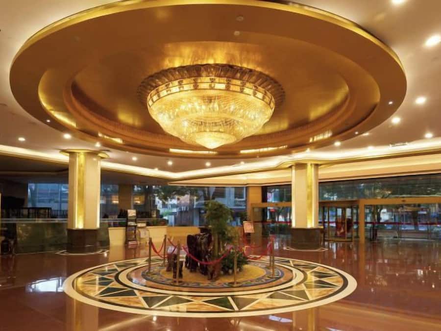 Um hall amplo com um design circular no chão, um lustre imponente e um elemento decorativo central.