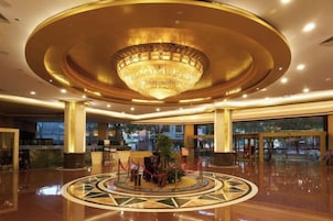 Um hall amplo com um design circular no chão, um lustre imponente e um elemento decorativo central.