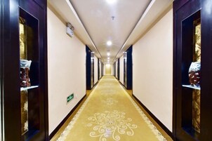 Corredor de hotel com piso coberto por carpete, portas em ambos os lados e luminária no teto.
